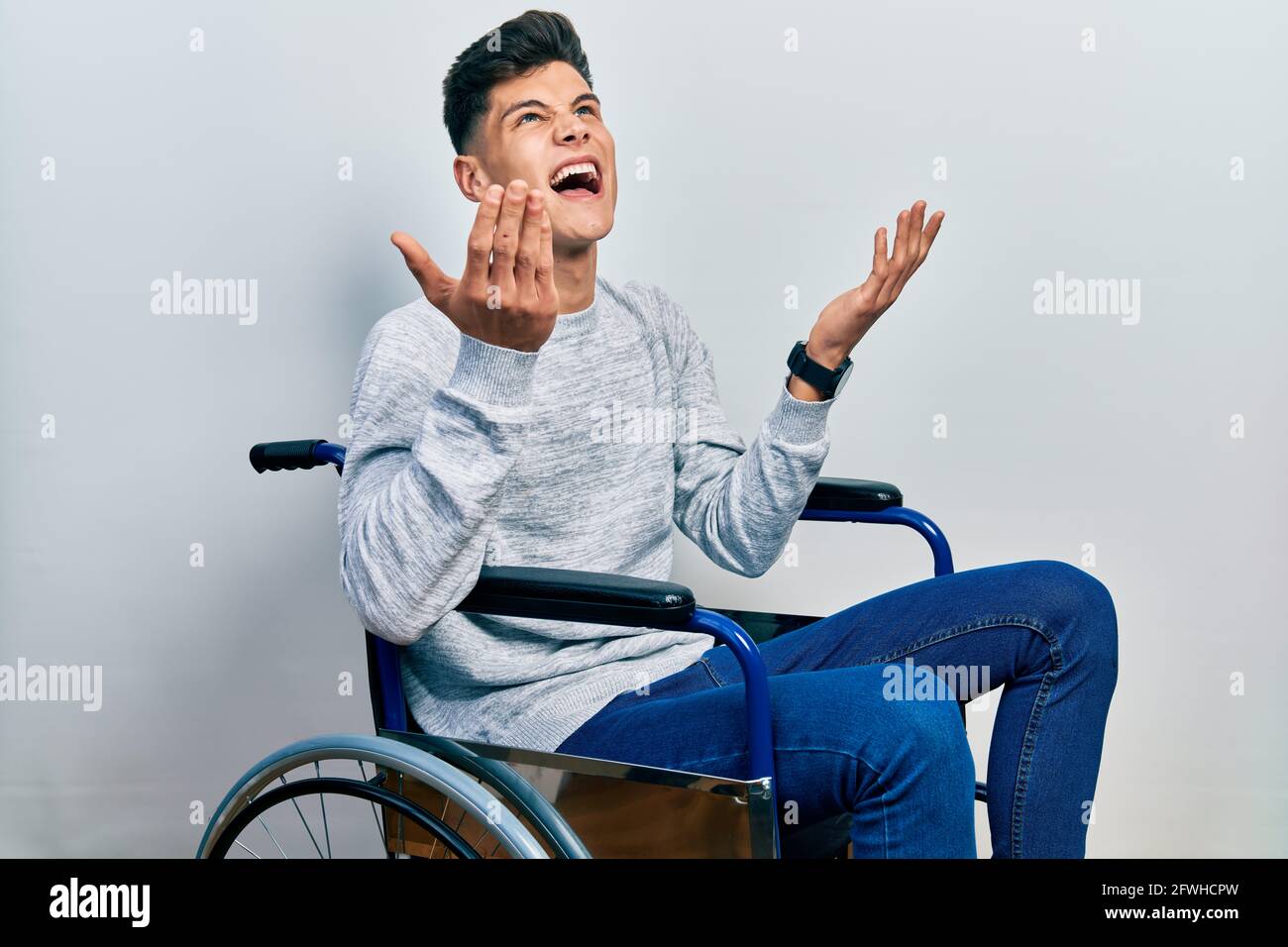 Young hispanic man sitting on wheelchair celebrating mad and crazy for ...
