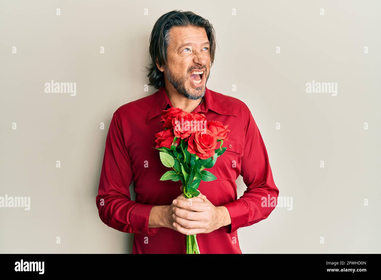 Middle age handsome man holding bouquet of red roses angry and mad ...