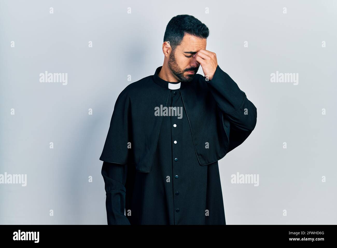 Handsome hispanic man with beard wearing catholic priest robe tired ...