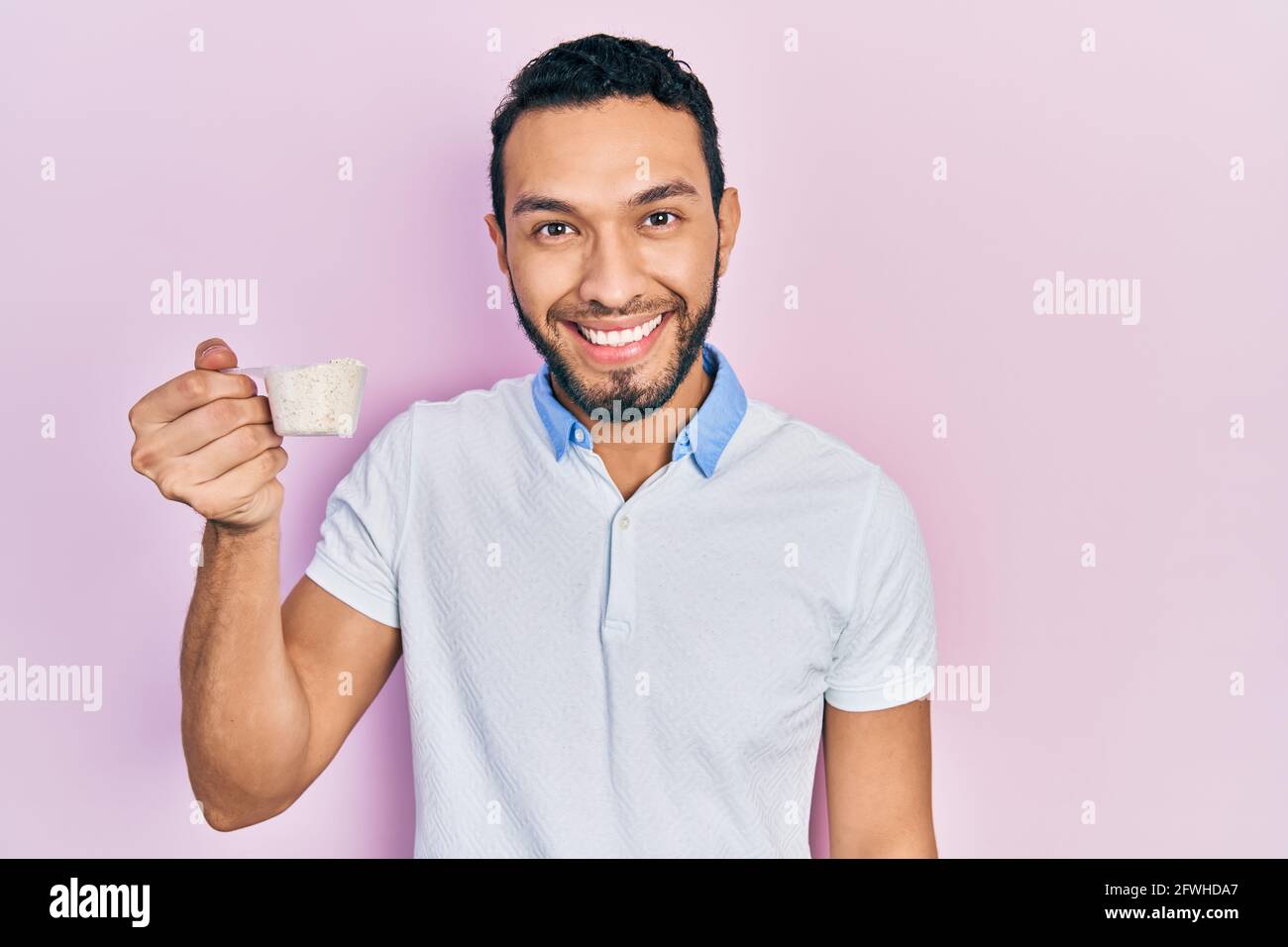 Hispanic man with beard holding white protein powder looking positive ...
