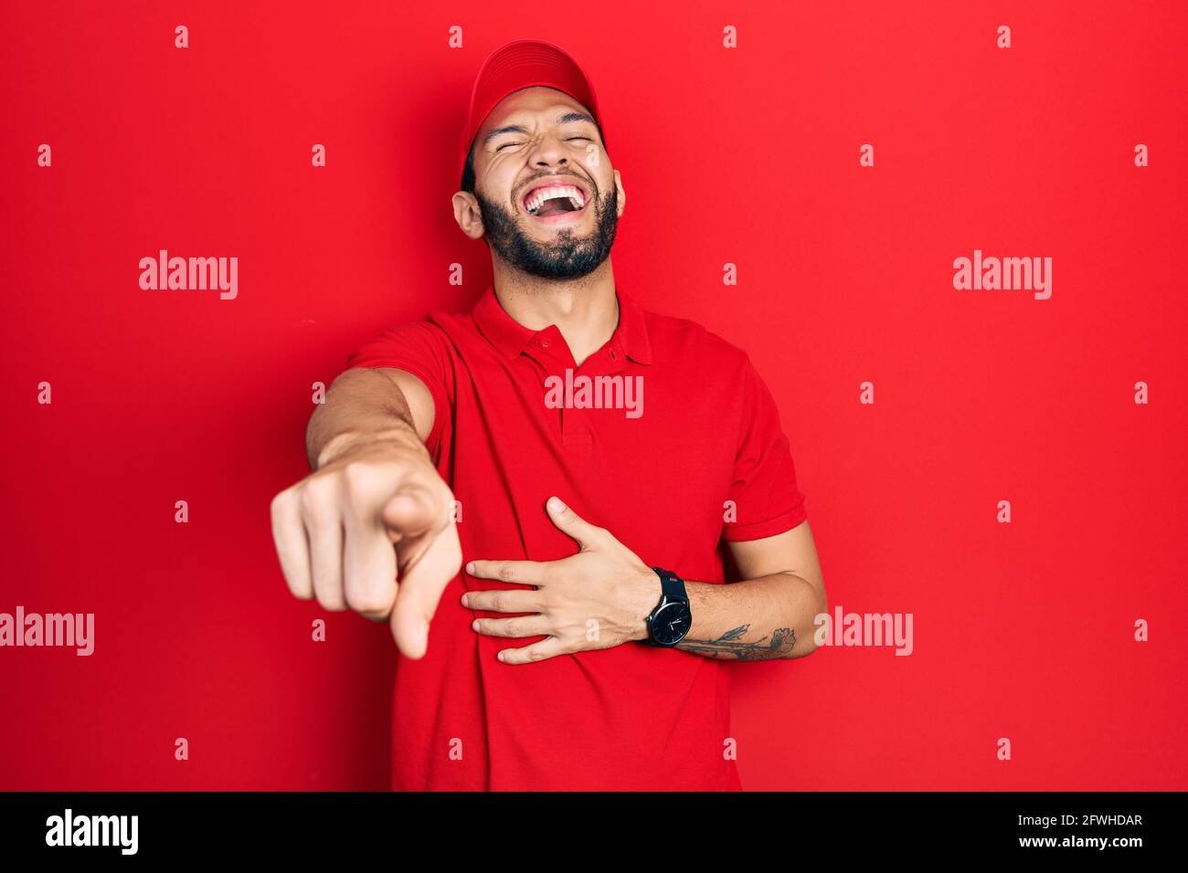 Hispanic Man With Beard Wearing Delivery Uniform And Cap Laughing At