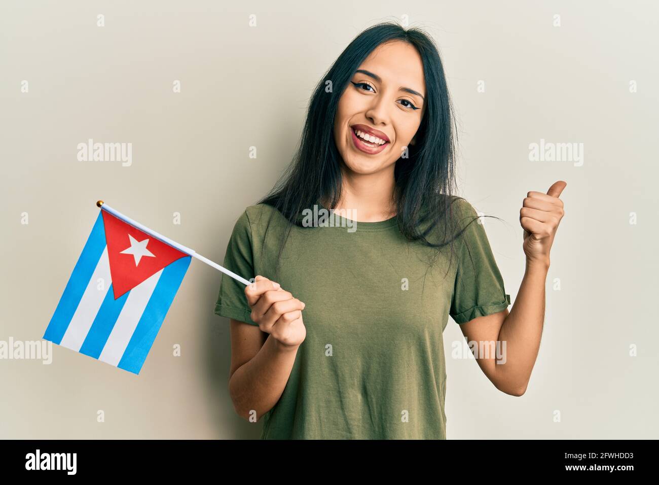 Young hispanic girl holding cuba flag pointing thumb up to the side ...