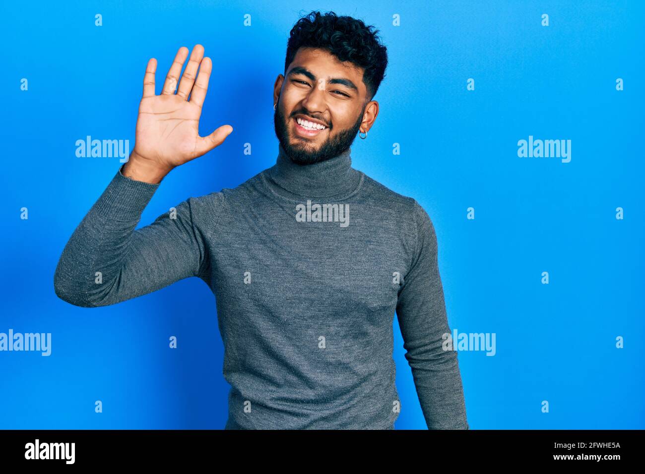 Arab man with beard wearing turtleneck sweater waiving saying hello ...