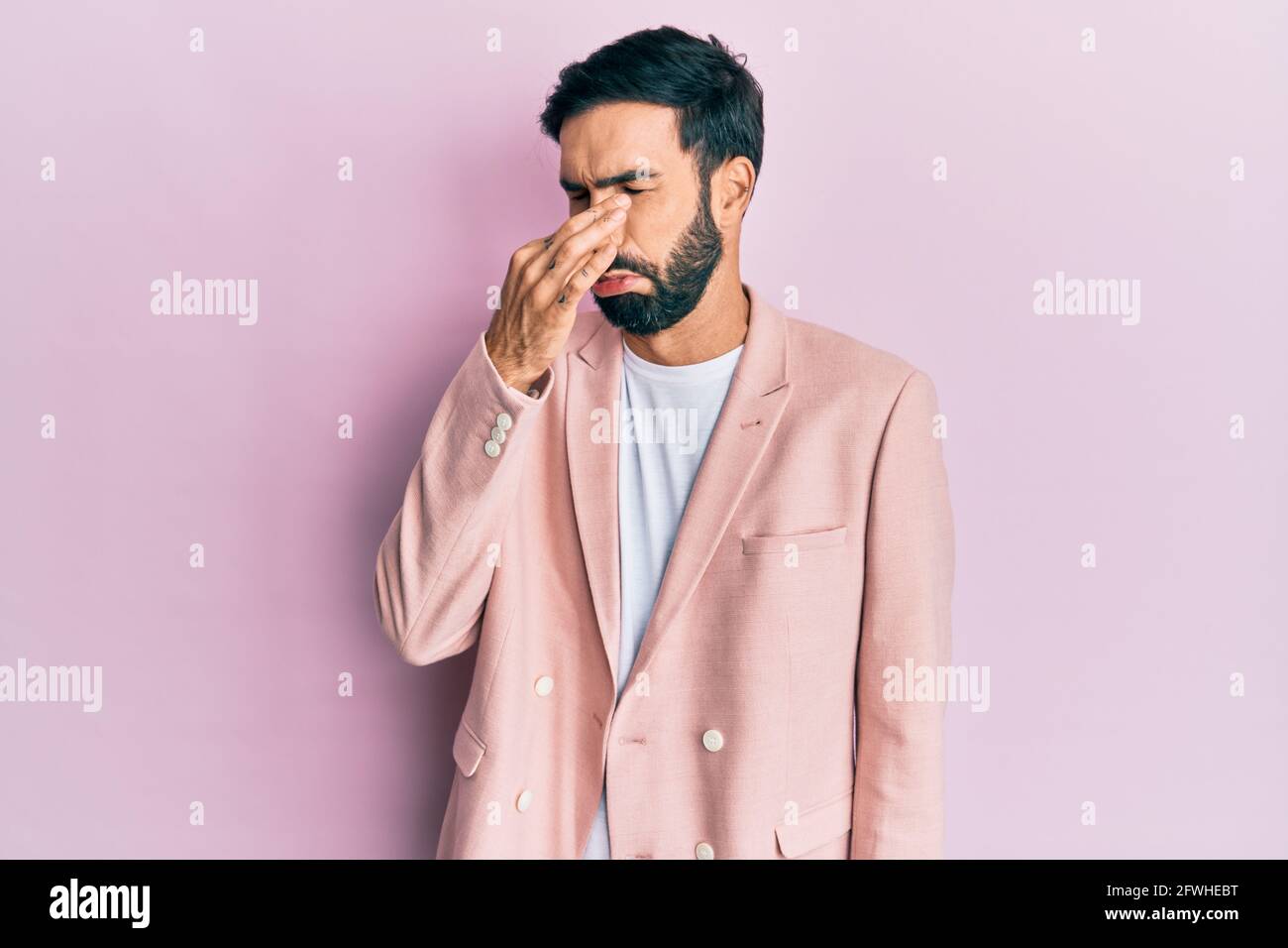 Young hispanic man wearing business jacket smelling something stinky ...