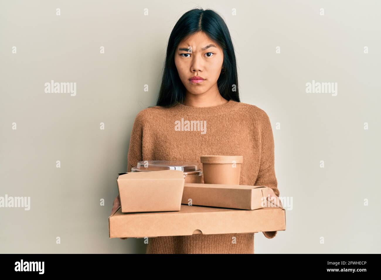 Young chinese woman holding take away food skeptic and nervous ...