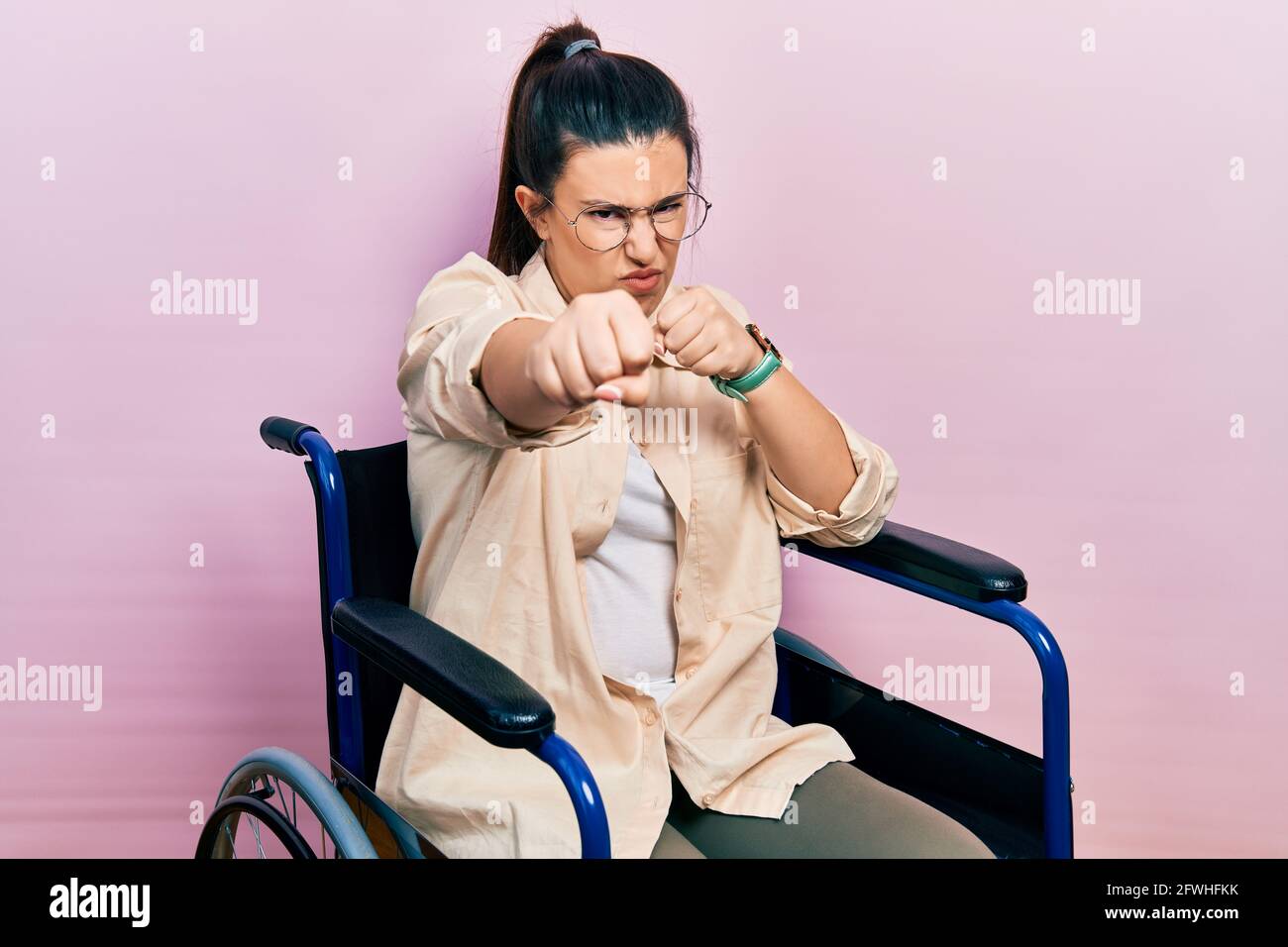 Young hispanic woman sitting on wheelchair punching fist to fight ...