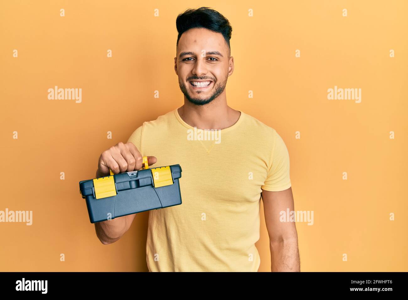 Young arab man holding toolbox looking positive and happy standing and ...
