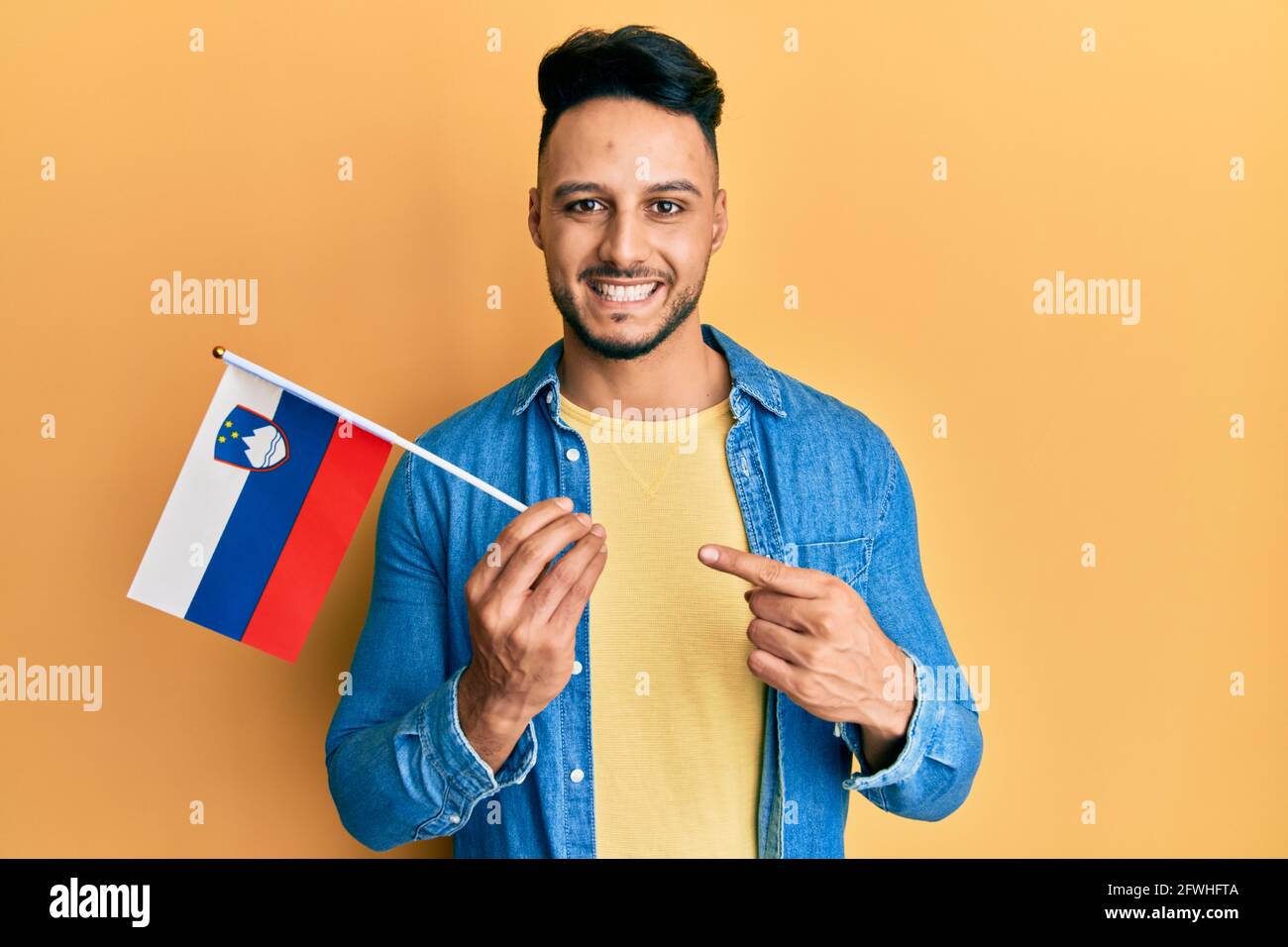 Young arab man holding slovenia flag smiling happy pointing with hand ...