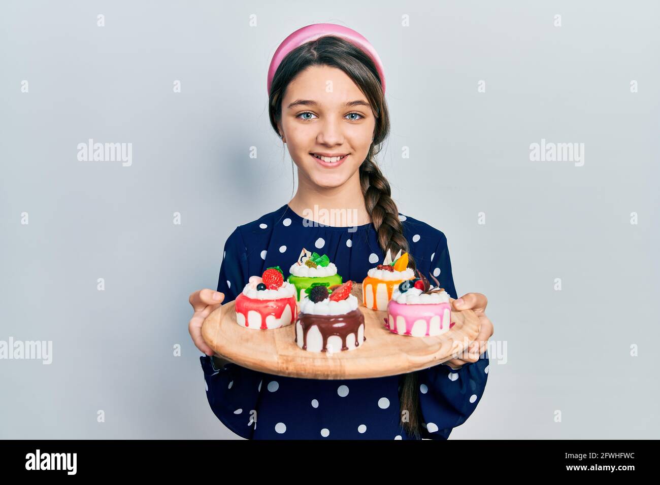 Young brunette girl holding sweet pastries smiling with a happy and ...