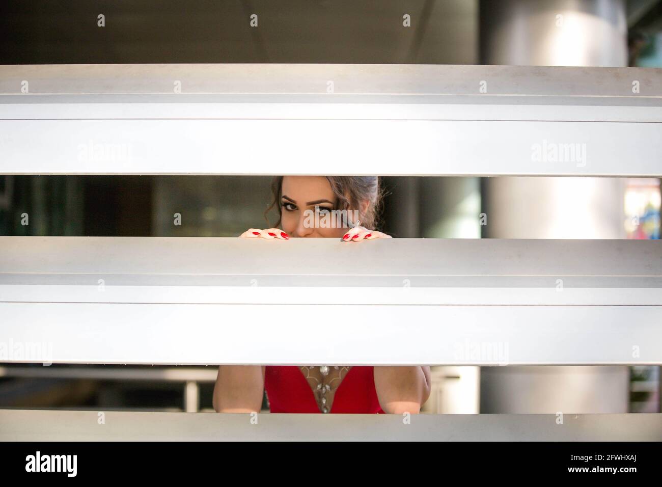 A shallow focus of a Caucasian woman in a red dress hiding behind the ...