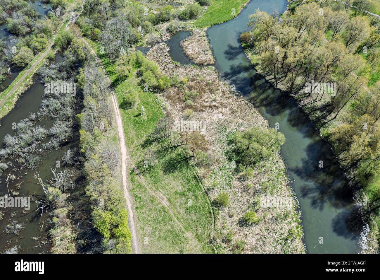 spring landscape with dirt road between wetlands and winding river at ...