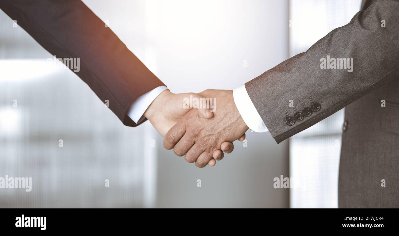 Business people standing and shaking hands in sunny office, close-up ...