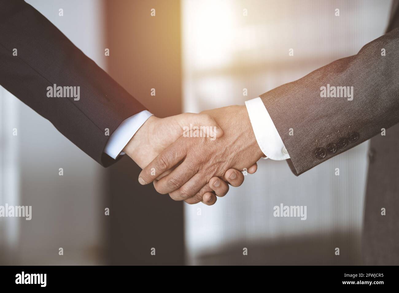 Business people standing and shaking hands in sunny office, close-up ...