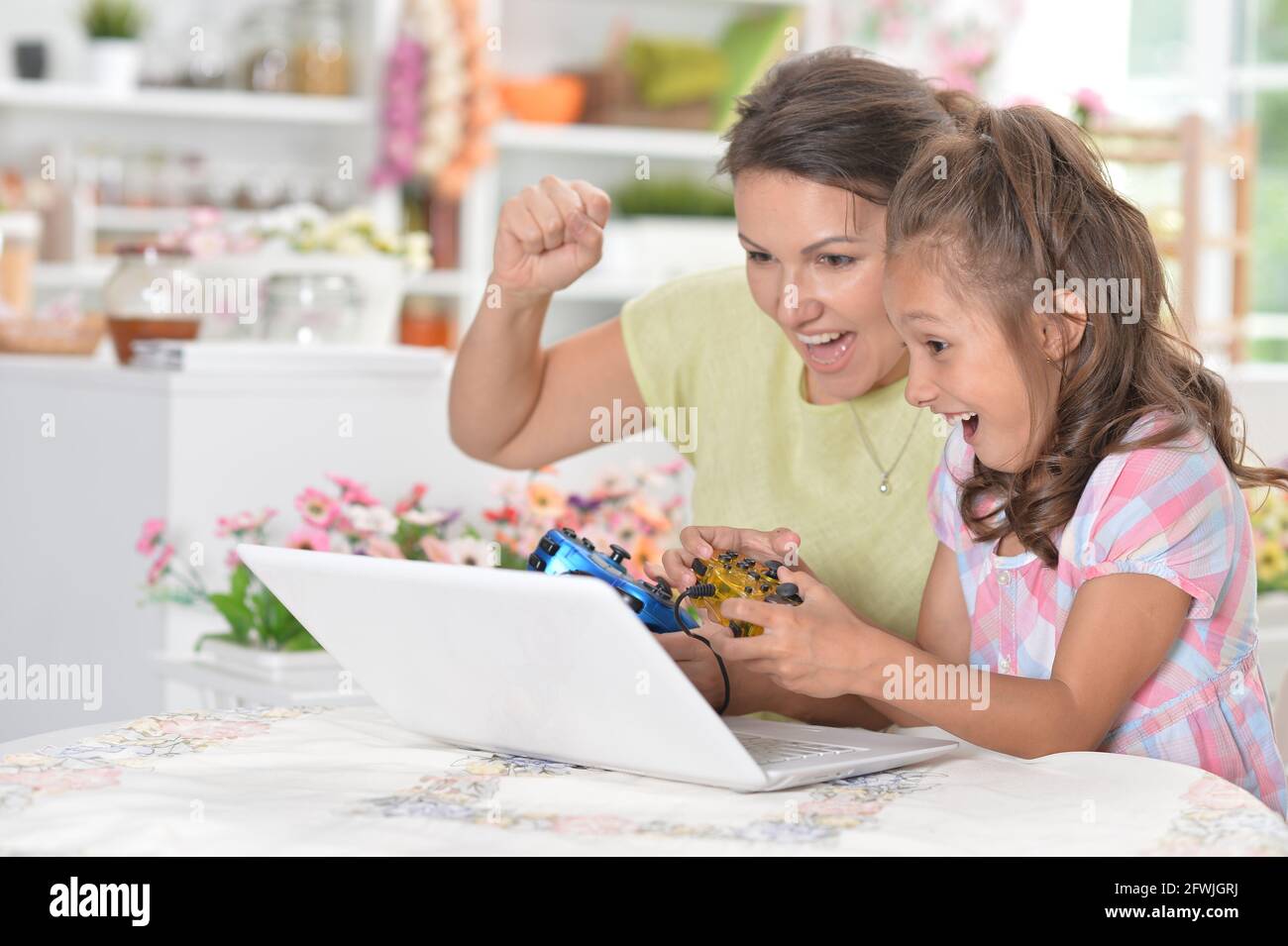 Cute girl with young mother playing computer game with laptop Stock ...