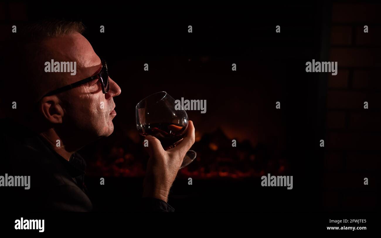 Mature man drinking cognac by the fireplace Stock Photo - Alamy