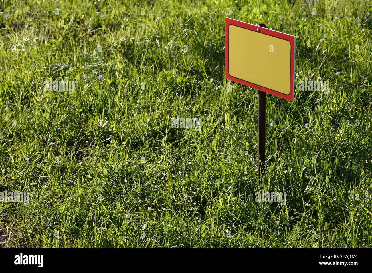 blank yellow one-legged sign mockup on green lawn background - close-up ...