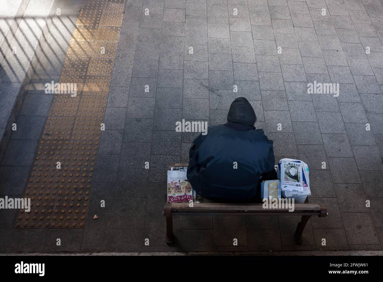 A homeless man reading as he rests on a bench in a small park in Tokyo ...