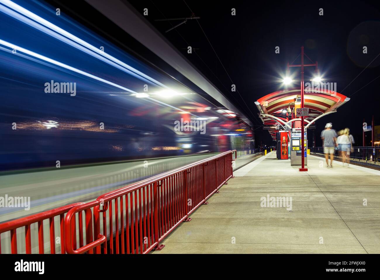 A light-rail train leaving the station with some passengers walking by ...