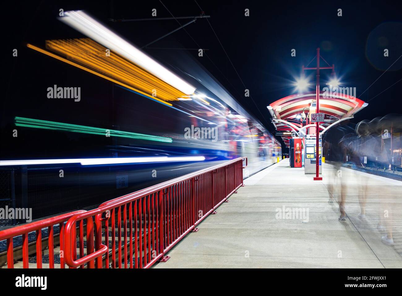 A light-rail train leaving the station with some passengers walking by ...