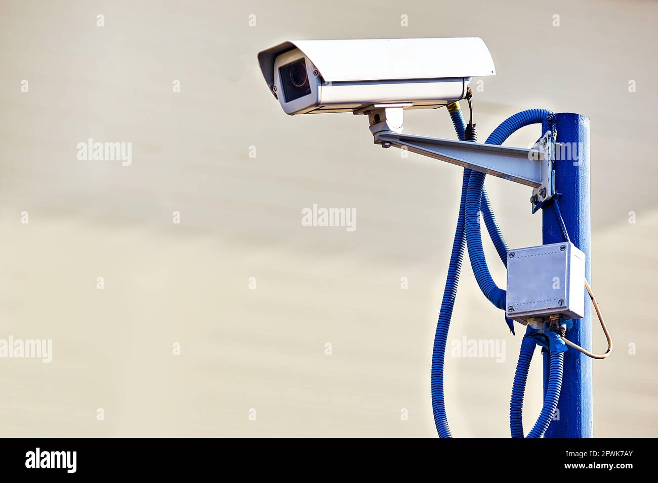 This is a security camera hanging on a pole on a summer day on a gray ...