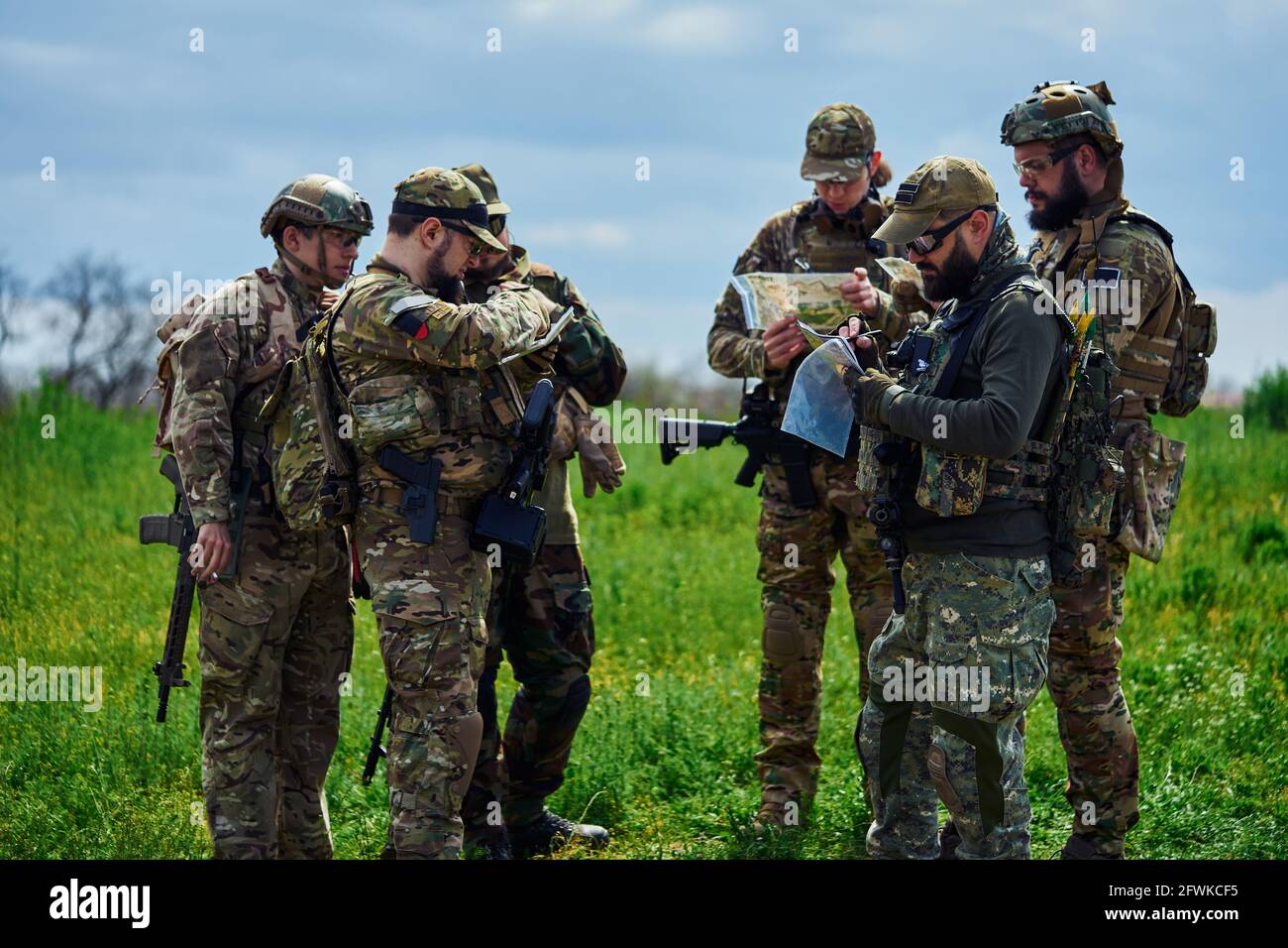 A group of airsoft players in military uniform are examining a map ...