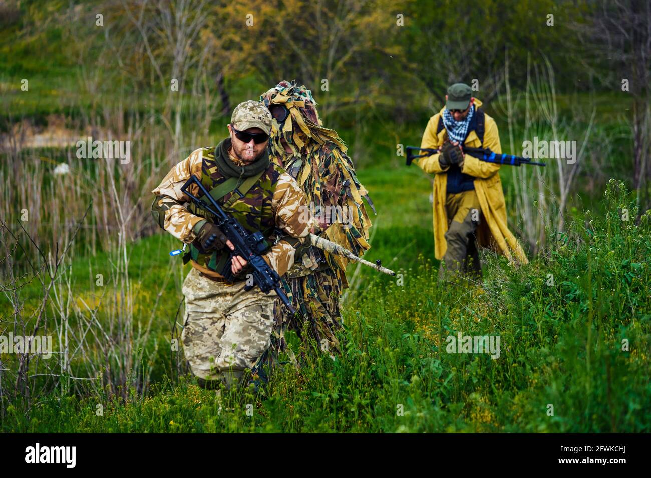 Airsoft players with weapons in their hands are walking in the forest ...
