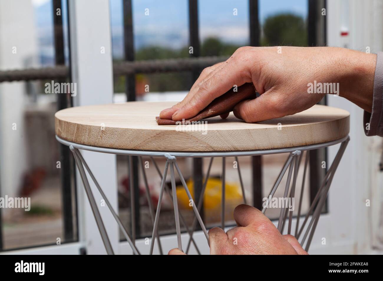 The hands of a carpenter sanding the wooden seat of a round stool with ...