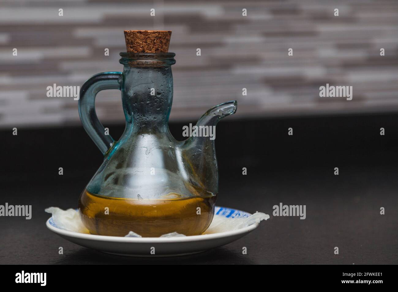 Olive oil in an oil can on a plate in a kitchen with black stone bench ...