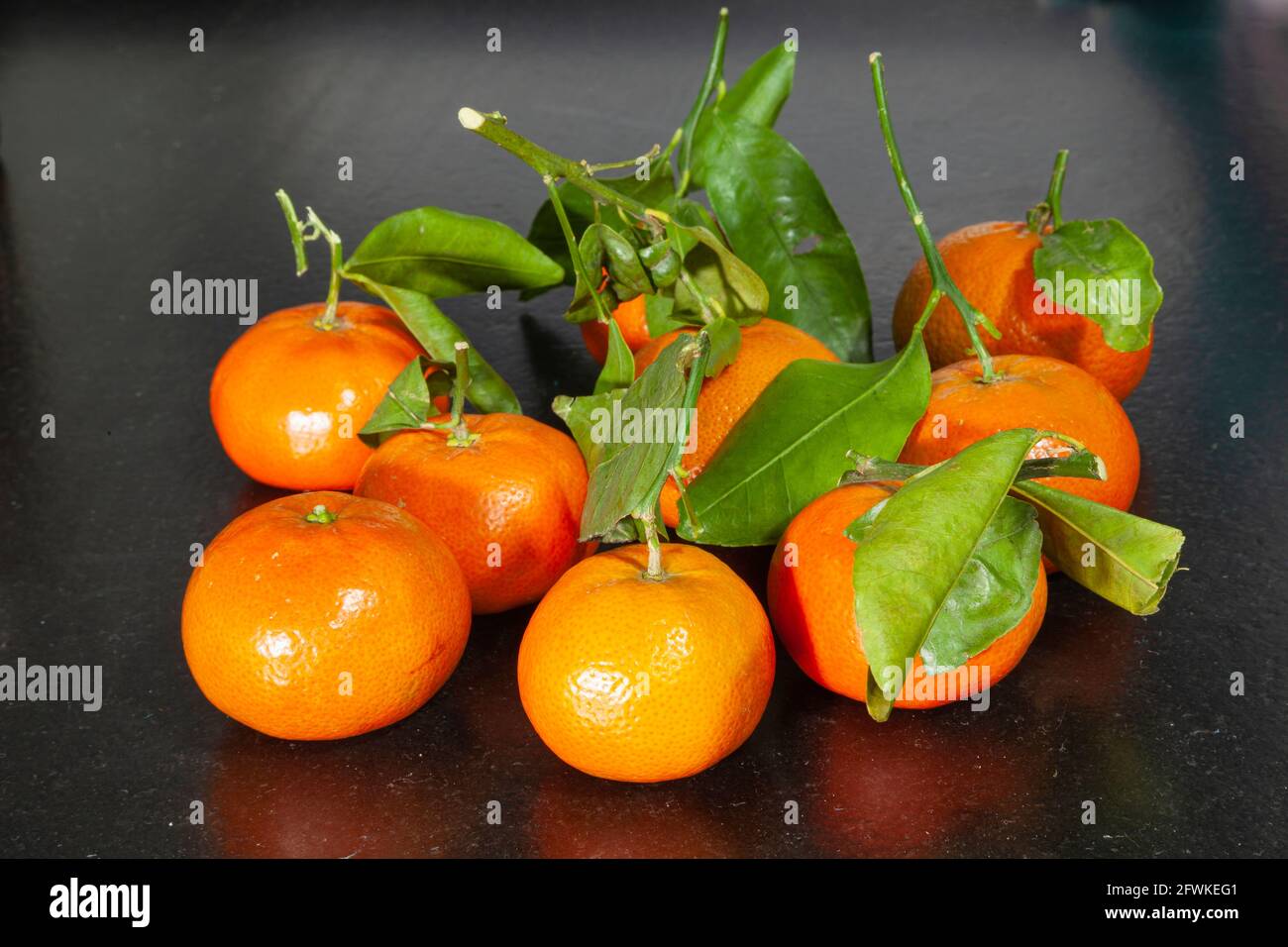 A handful of tangerines with stem and leaves placed on a black granite ...