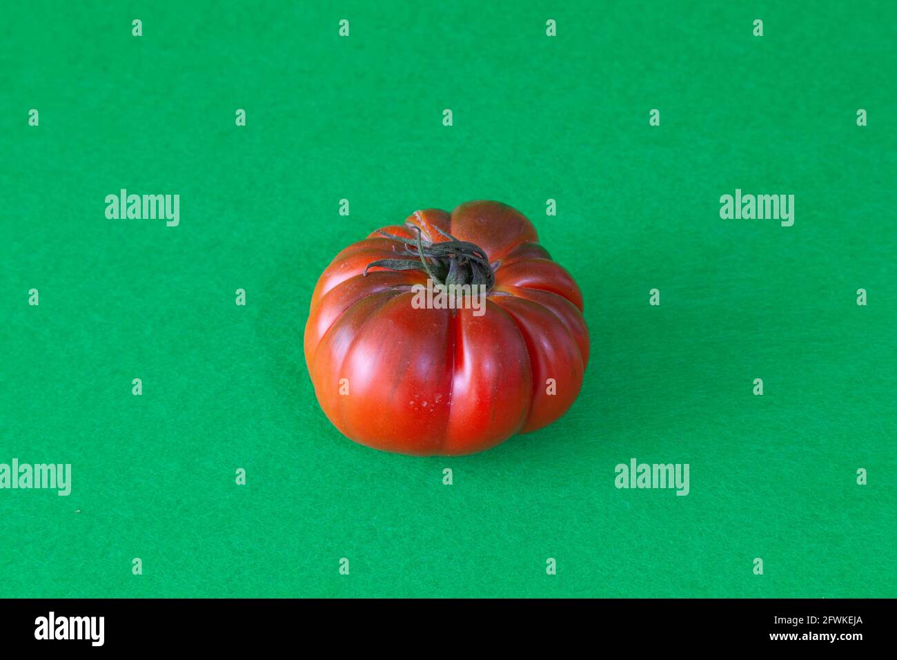 Red tomato of the raft variety isolated on a green background. The ...