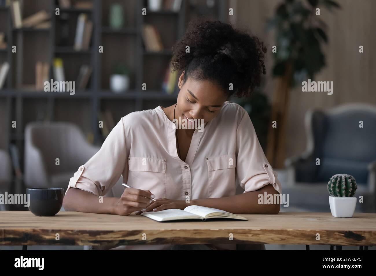 Smiling young mixed race businesswoman writing notes in paper planner ...