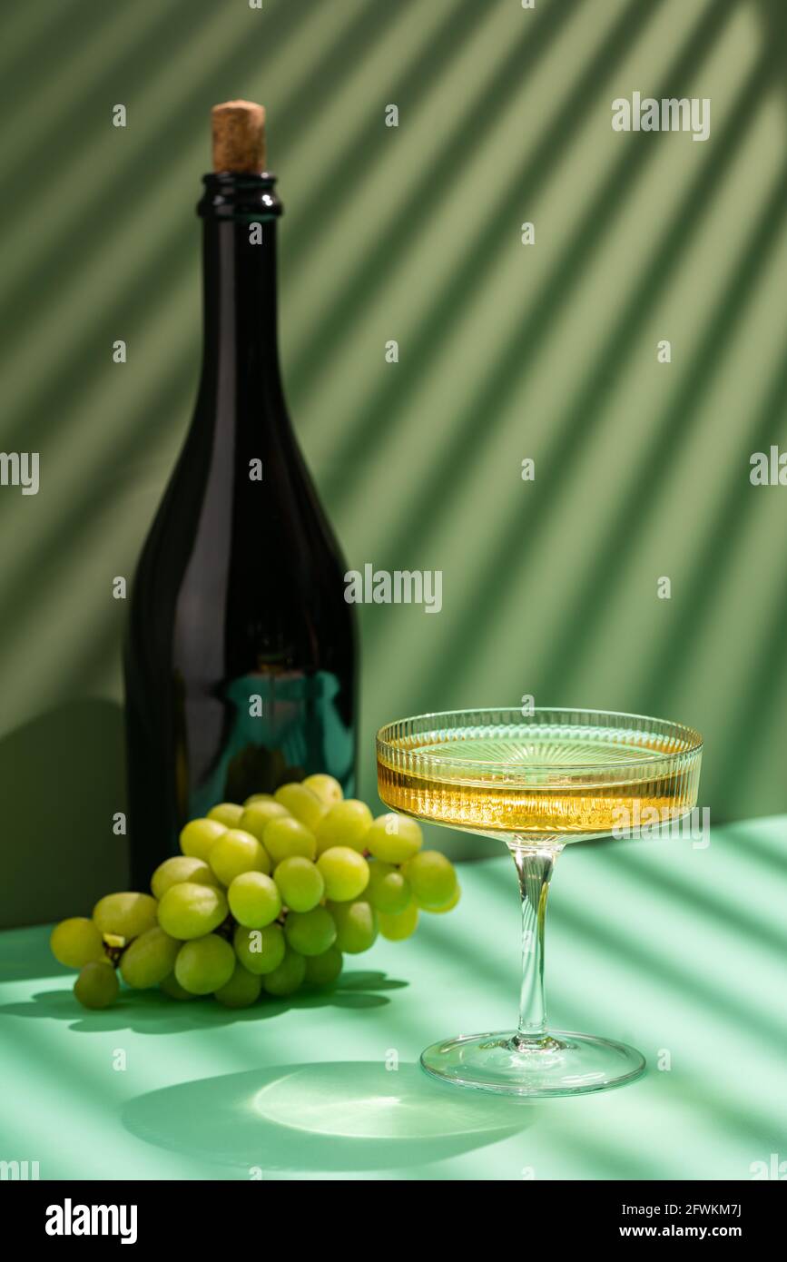 Wine Glass and bottle of white wine with bright shadows over green ...