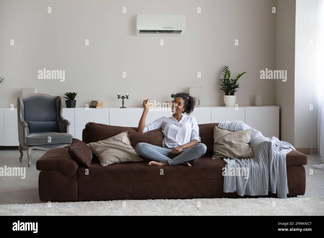 Relaxed smiling african woman turning on air conditioner Stock Photo ...