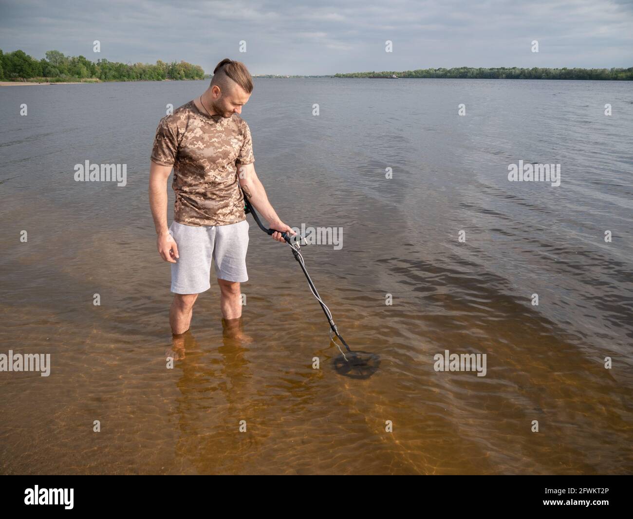 Guy in the river is looking for treasure with a metal detector in the ...