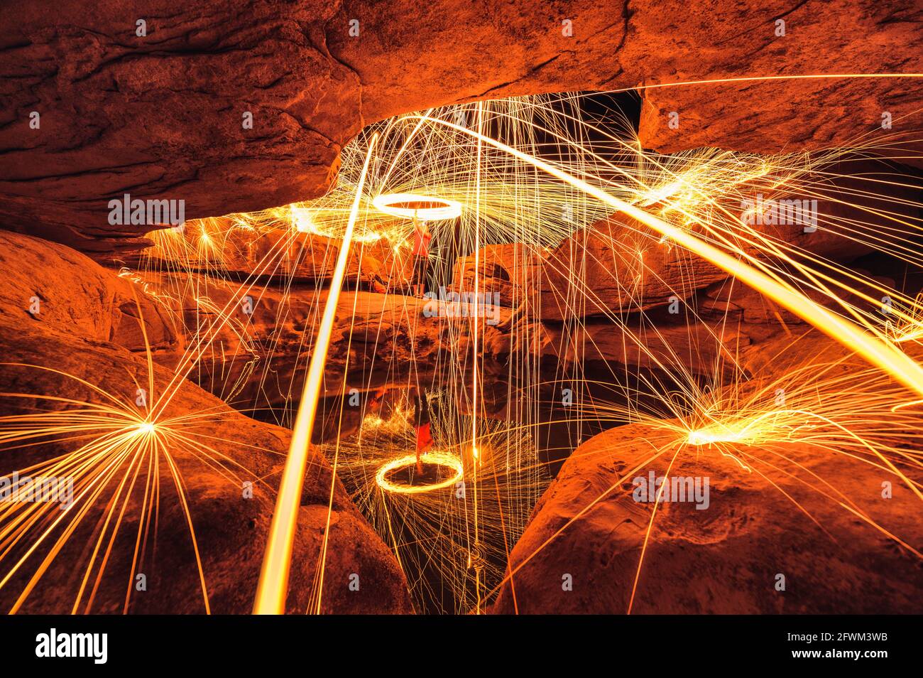 Man wielding spark fire swirl in stone hole cave and pond reflection in ...