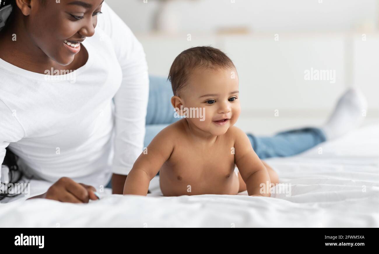 Cute little African American baby crawling in bed with mom Stock Photo ...