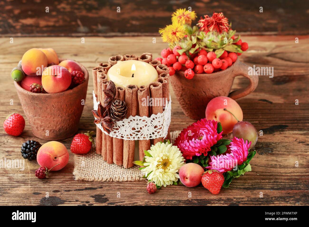 Candle decorated with cinnamon sticks among autumn fruits and flowers ...