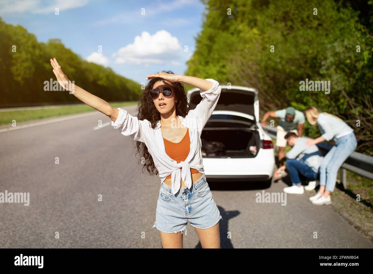 Young woman trying to wave down car, asking for help, her friends ...