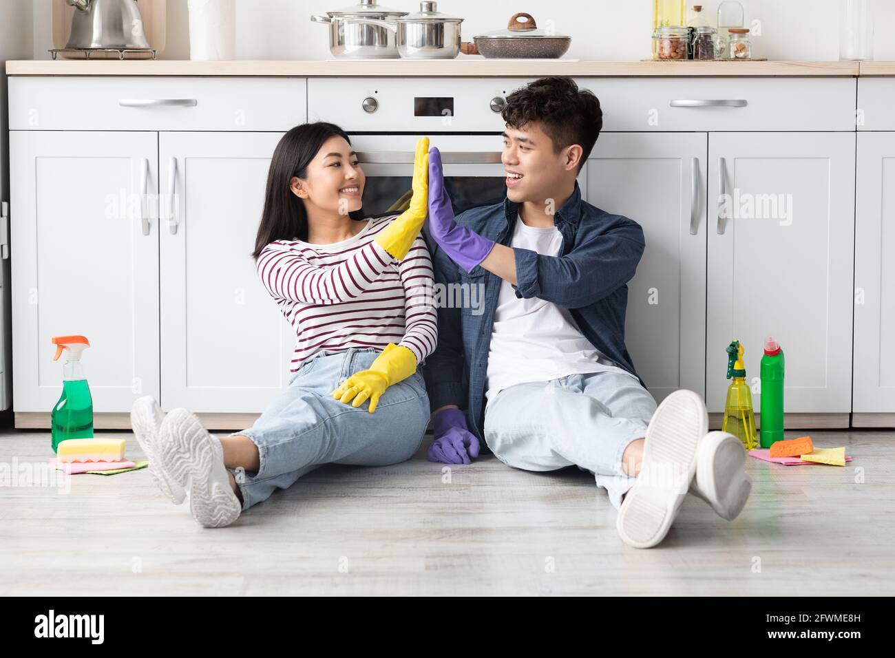 Tired asian couple sitting in kitchen, giving high five Stock Photo - Alamy
