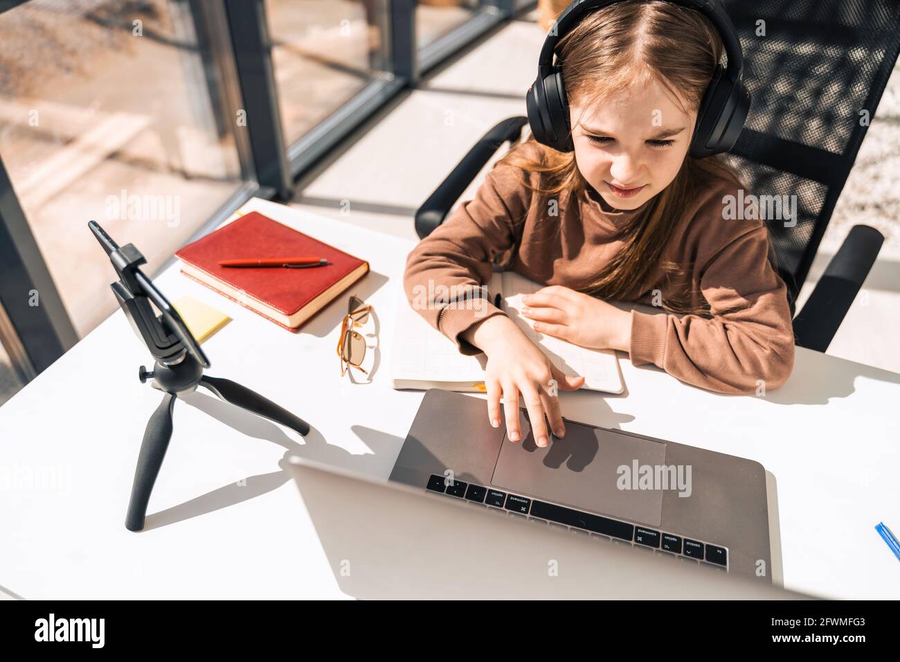 Cute schoolgirl in headphones works at laptop. Little girl study online ...