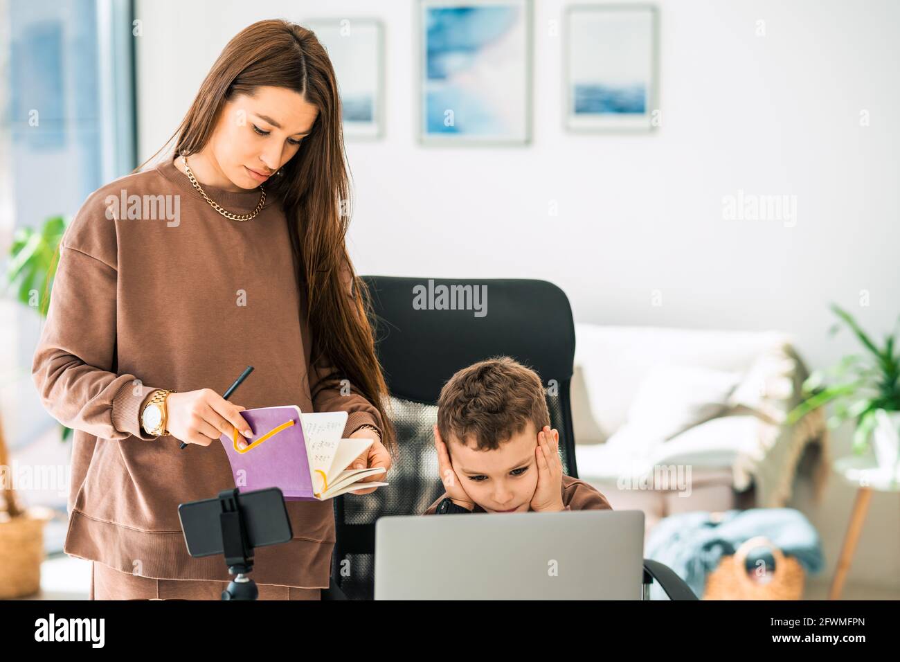 Mother looks in the school diary of her son. Sad boy doing homework on ...