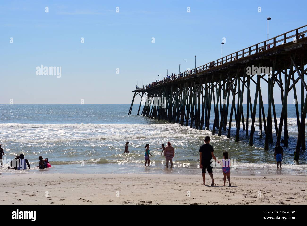 Beach-goers cool off in the ocean next to the pier at Kure Beach, North ...