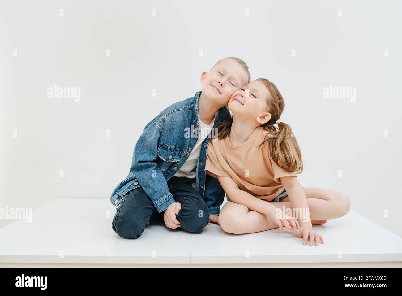 Cuddling siblings sitting on table, pressing cheeks in bliss, love and ...
