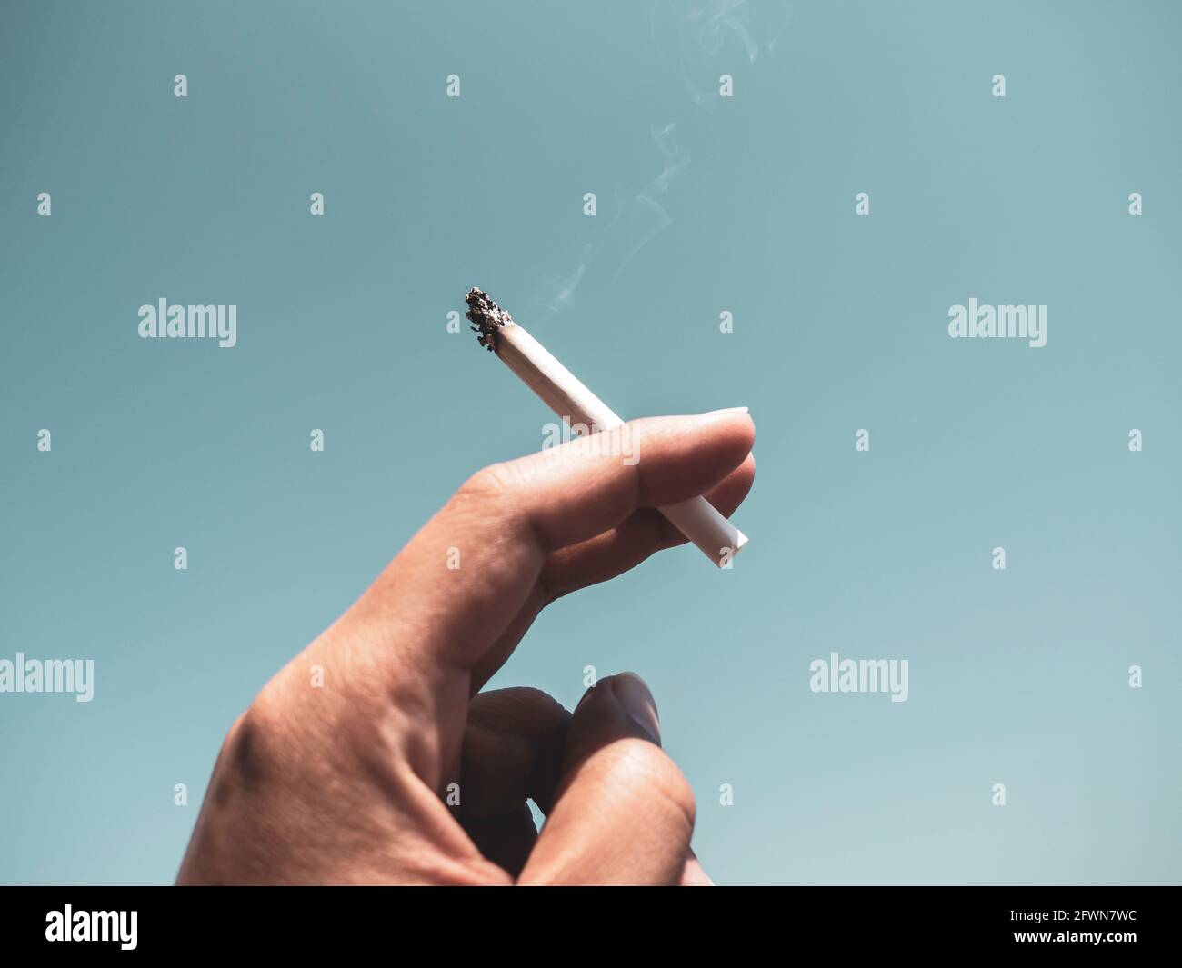Cigarette in man hand with smoke on blue sky background. Hand holding ...