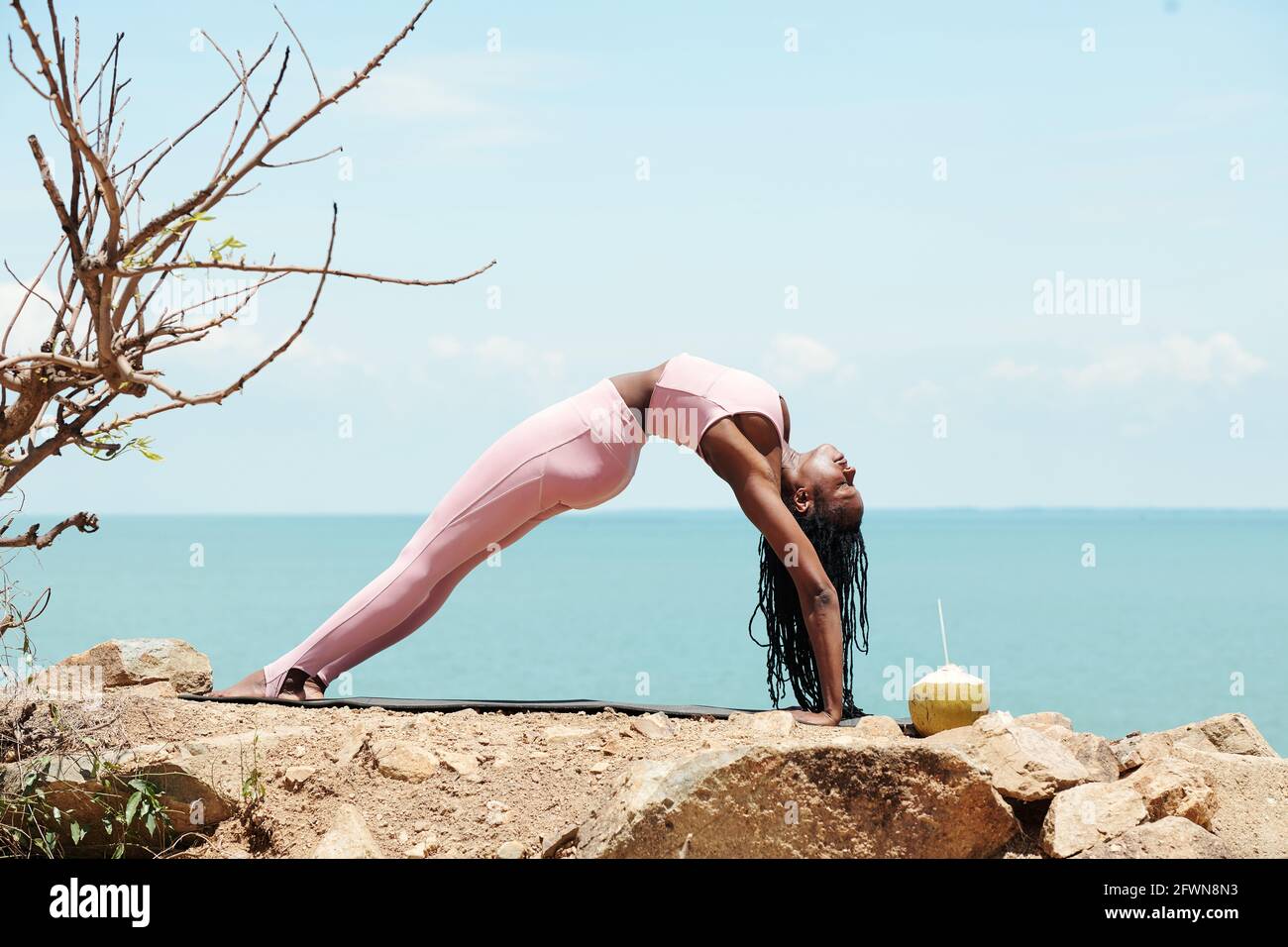Fit strong young woman doing upward bow pose when working out on beach ...