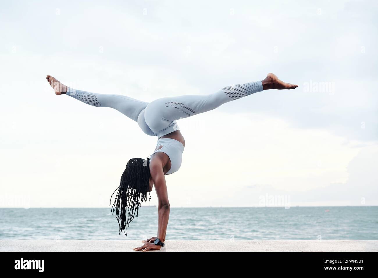 Side view of athletic young woman practicing yoga, doing handstand with ...