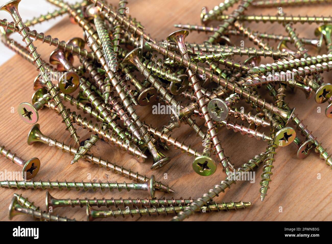 Close-up of scattered large long new tapping screws on light brown wood ...