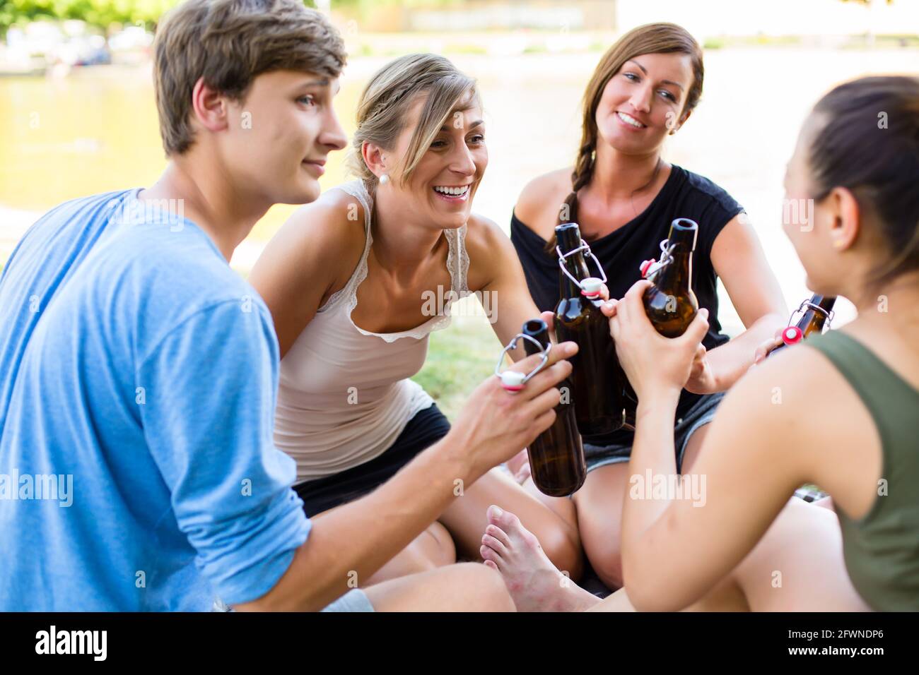 Students in park toasting with beer bottles having picnic at river ...