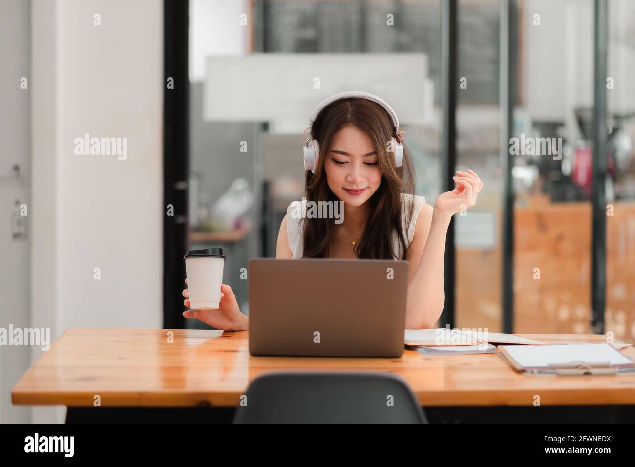 Concentrated young asian female wearing headphone and look at laptop ...