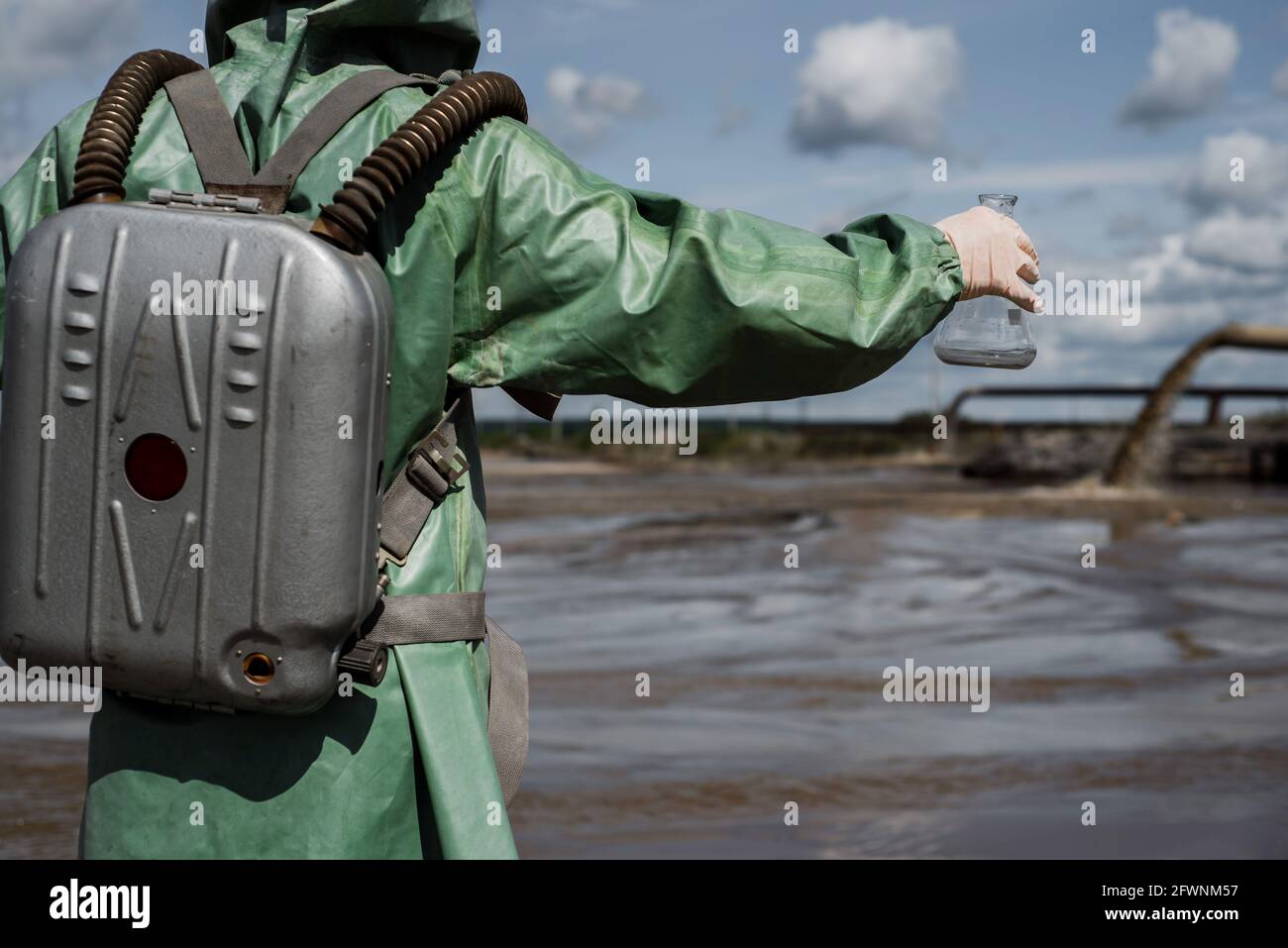 A male environmentalist in a green protective suit and gas mask takes a ...